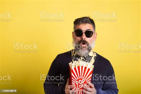 선글라스를 쓰고 팝콘을 먹는 수염난 남자는 노란 배경에 있는 영화를 보고 깜짝 놀랐다 노랑에 대한 스톡 사진 및 기타 이미지