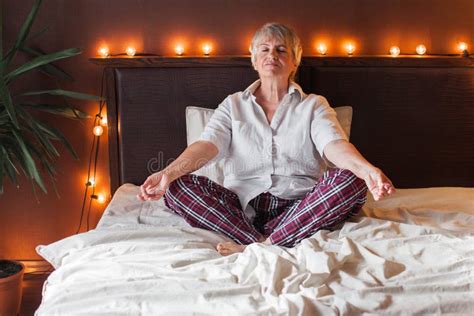 Middle Aged Woman Sitting In Lotus Meditating At Morning In Bedroom