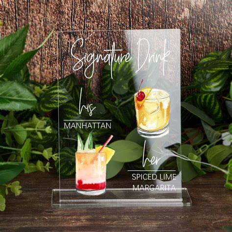 An Acrylic Sign With Cocktails On It Sitting In Front Of Some Plants