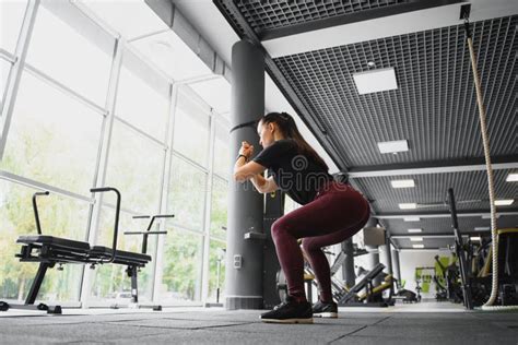Side View Portrait Of A Young Woman Doing Squats At Fitness Gym Stock