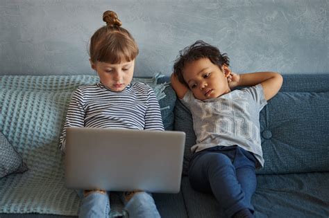 작은 아프리카 소년과 백인 소녀는 소파에 앉아 디지털 태블릿에 게임을 집에서 노트북에서 만화를 보고 있는 아이들 현대 어린이 및 교육 기술 공부에 대한 스톡 사진 및 기타