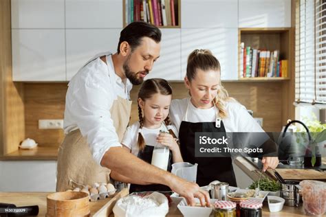 앞치마에 행복한 가족이 피자 재료를 보며 이야기하는 이야기 수제 반죽을 반죽하기 위해 밀가루를 먹는 아버지는 우유 관찰 과정을 들고있는 호기심 많은 딸 음식을 섞는 금발