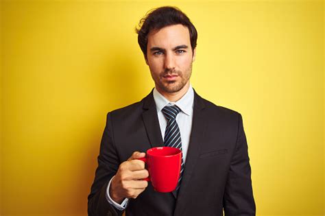 젊은 잘 생긴 사업가 는 심각한 생각 스마트 얼굴에 자신감 표정으로 고립 된 노란색 배경 위에 커피의 빨간 컵을 마시는 감정에 대한 스톡 사진 및 기타 이미지 Istock