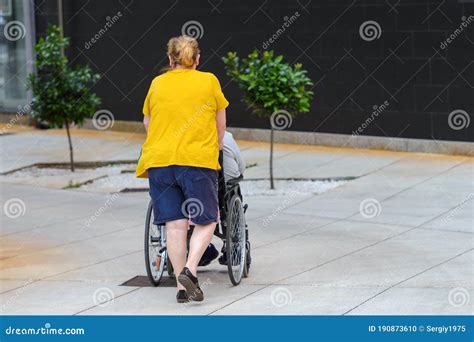 Unrecognizable Woman Pushing A Wheelchair With A Disabled Person
