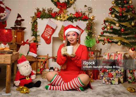 산타클로스 모자와 줄무늬 양말을 신은 빨간 옷을 입은 여자가 크리스마스 세트에 앉아 있는 흰색 머그잔을 들고 있다 30 34세에 대한 스톡 사진 및 기타 이미지 Istock