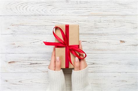 여자 손에 빨간 리본으로 종이에 포장된 발렌타인 또는 다른 휴일 수 제 선물을 제공합니다 선물 상자 흰색 나무 테이블 복사 공간 평면도에 선물의 장식 Diy에 대한 스톡