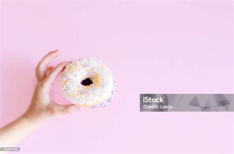 분홍색 배경에 화려한 흰색 도넛을 손에 들고 있는 여성을 닫습니다 적절한 영양 또는 과자 디저트 패스트 푸드 다이어트 아침 개념 광고를위한 공간을 복사하십시오 광고 영역