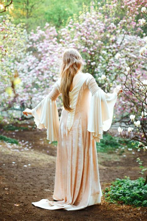 A Woman With Long Hair In A White Dress Is Walking Through A Garden