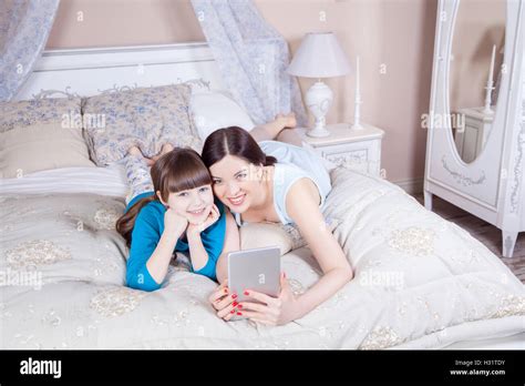 Glückliche Mutter und Tochter lag im Bett mit digital Tablette lächelnd und Blick in Kamera
