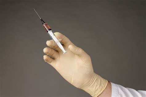 Рука с латексной перчаткой держащей шприц с вакциной Бесплатно Фото