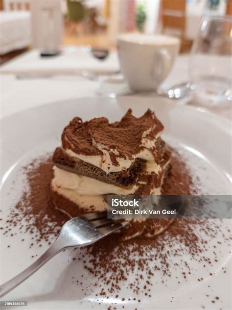 이탈리안 레스토랑의 테이블 위에 놓인 하얀 접시에 담긴 티라미수 그 옆에 작은 포크가 있습니다 맛있는 이탈리안 디저트 배경에 있는 레스토랑 인테리어 0명에 대한 스톡 사진