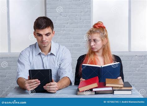 Парень читает Ebook и девушка сидит на куче различных книг и Gazing с