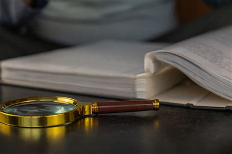 열린 파일 폴더 옆에 있는 돋보기입니다 금색 프레임이있는 둥근 돋보기가 검은 책상 위에 놓여 있습니다 바인더가 있는 회색 파일