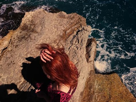 Premium Photo Redhead Woman Sitting On Rock At Beach