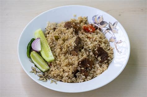 나무 배경에 오이 조각 양파 청양고추를 곁들인 흰색 접시에 맛있는 쇠고기 테하리 쌀과 쇠고기로 만든 방글라데시 전통 요리입니다