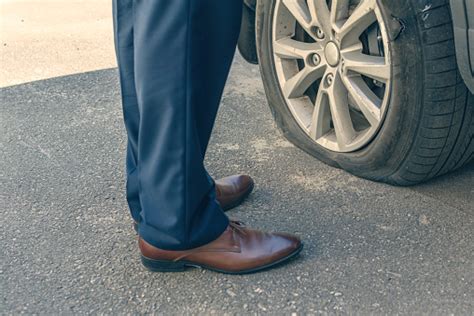 파란색 양복을 입은 사업가가 차 근처에 서서 바퀴에 구멍이 뚫린 정도정도를 확인한다 타이어에 구멍 개념 견인차에 대한 스톡 사진 및 기타 이미지 Istock