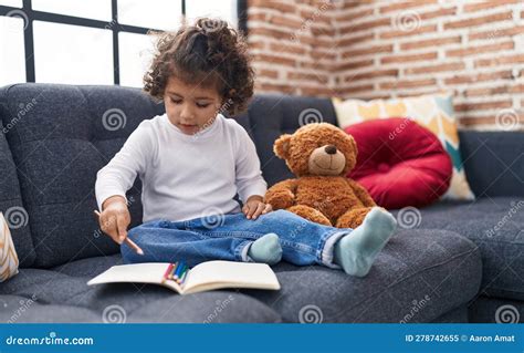 Adorable Hispanic Girl Drawing On Notebook Sitting On Sofa At Home