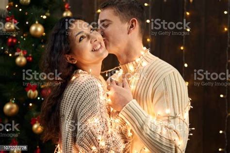 젊은 부부는 크리스마스 장식 및 조명 어두운 나무 배경 새 해 휴일 개념에 전나무 나무에 갈란드 장식품에 대한 스톡 사진 및