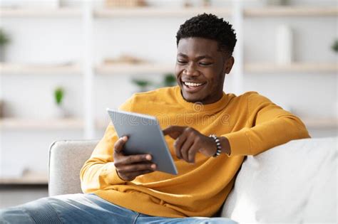 Smiling African American Man Sitting On Couch With Digital Tablet Stock