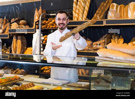 Happy Male Shop Assistant Demonstrating Delicious Loaves Of Bread In