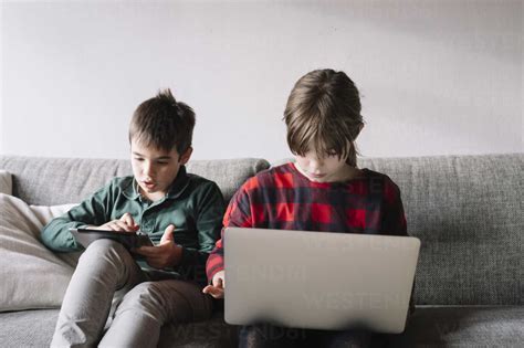 Bruder und Schwester sitzen auf der Couch im Wohnzimmer und benutzen mobile Geräte lizenzfreies