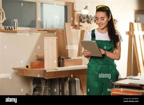 Professional Carpenter In Uniform With Tablet Near Workbench Stock