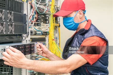 의료 용 마스크 전문가가 서버실에서 장비를 유지합니다 빨간색 모자를 쓴 남자가 데이터 센터에서 작동합니다 기술자는 격리 중에 새