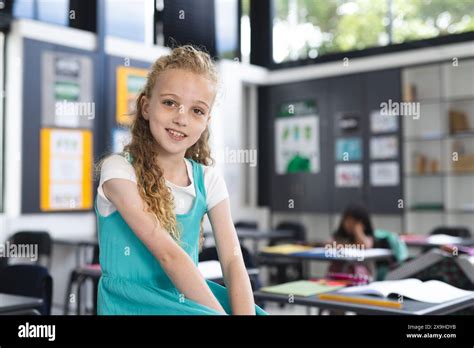 Caucasian Girl With Curly Blonde Hair Smiles In A School Classroom With