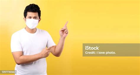 마스크를 쓰고 잘 생긴 아시아 남자의 초상화는 복사 공간 스튜디오에서 노란색 배경에 고립 된 아픈 포인팅 손가락입니다 건강관리와 의술에 대한 스톡 사진 및 기타 이미지