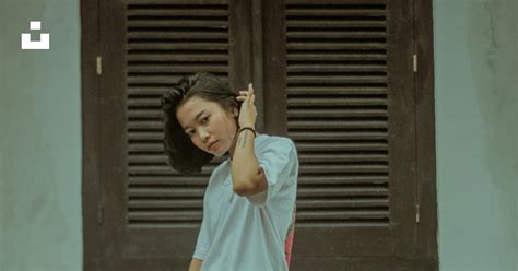 흰색 티셔츠와 검은색 반바지를 입은 소녀가 갈색 나무 문 옆에 서 있다 사진 Unsplash의 무료 사람의 이미지