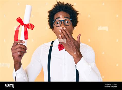 Handsome African American Nerd Man With Afro Hair Holding Graduate Degree Diploma Covering Mouth