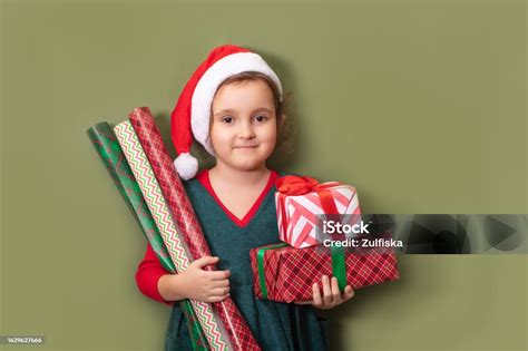 산타 모자를 쓴 귀여운 백인 아이 유아 소녀는 녹색 배경에 포장지가 있는 선물 상자를 들고 있다 디자인 또는 텍스트를 위한 공간을 복사합니다 기치 크리스마스 새해 모형