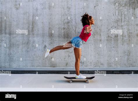 Multiracial Teenage Girl Riding A Skateboard In Front Of Concrete Wall