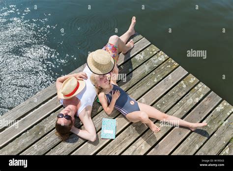 Mother And Daughter Lying On Swimming Platform Reading Sunbathing