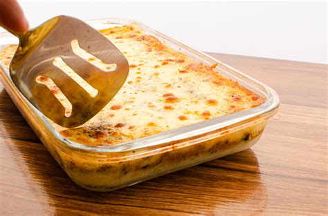 유리 플래터에 라자냐를 자르는 손 요리 개념 나무 테이블에 라자냐 요리의 구성 Lasagna는 리본을 겹겹이 놓고 채우기와