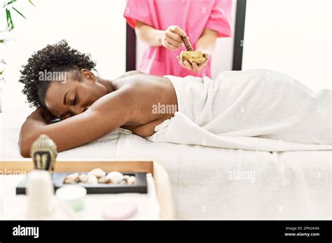 African American Woman Lying On Table Having Back Massage Using Cream