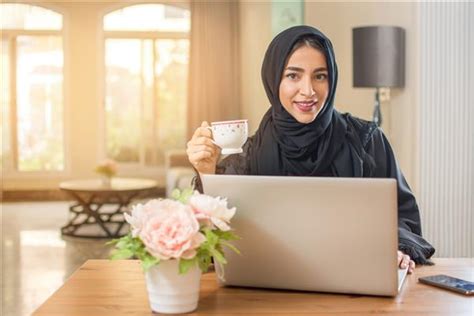 زن جوان عرب با فنجان قهوه با استفاده از لپ تاپ و نگاه کردن به دوربین 1636408