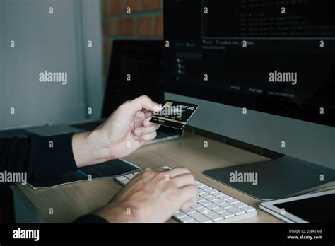 Hacker In The Hood Working With Computer And Holding Credit Card With