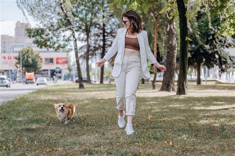 하얀 양복과 선글라스를 착용하고 웨일스 어 코기 펨브로크 개와 함께 도시 공원에서 걷는 행복한 여성 개에 대한 스톡 사진 및 기타 이미지 Istock