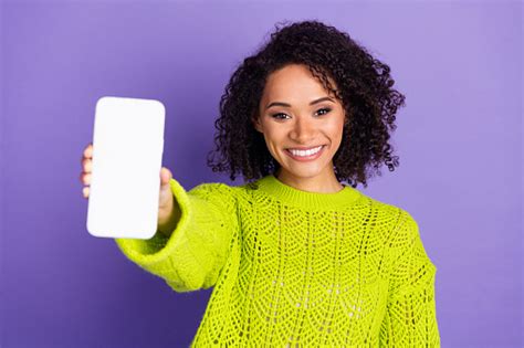 녹색 스웨터를 입은 곱슬 곱슬 한 미국 젊은 펑키 소녀의 사진은 자주색 배경에 격리 된 스마트 폰 디스플레이 다운로드 응용 프로그램을 보여줍니다 20 24세에 대한 스톡