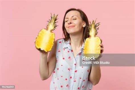 눈을 감고 여름 옷에 어린 소녀 웃는 분홍색 파스텔 배경에 고립 된 신선한 잘 익은 파인애플 과일의 Halfs를 유지 합니다 사람들은 생생한 라이프 스타일 휴식 휴가