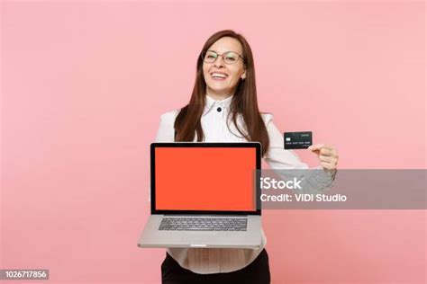 분홍색 배경에 고립 된 빈 빈 화면으로 신용 카드 노트북 Pc 컴퓨터를 들고 안경에 젊은 웃음 비즈니스 여자 여자 보스입니다