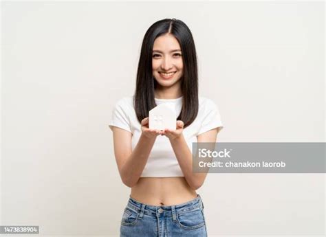 고립 된 흰색 배경에 서있는 집 조롱을 들고 젊은 귀여운 아시아 여성 부동산 및 주택 보험 개념 집 샘플 모델을 가진 비즈니스
