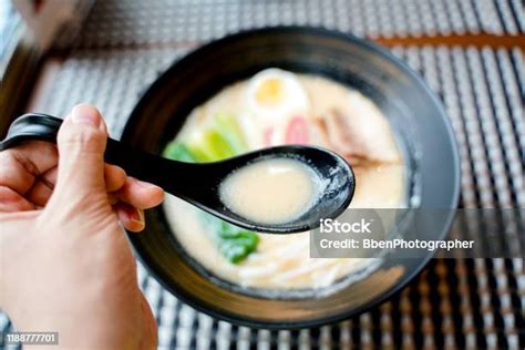 숟가락을 들고 숟가락 안에 라면 수프 부드러운 흐림 은 검은 그릇에 라멘에 초점을 맞추고 일식 레스토랑에서 테이블에 제공됩니다