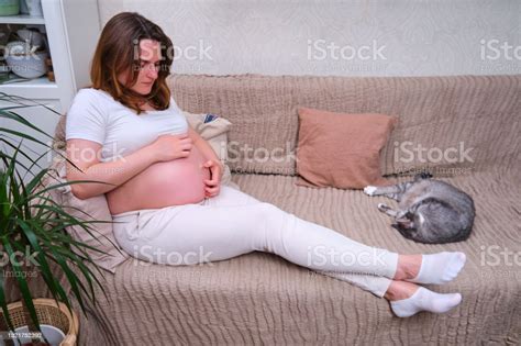 Pregnant Woman Scratches Her Stomach While Sitting On The Home Sofa In ...