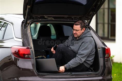 Un Hombre Sentado En El Maletero Abierto De Un Auto Y Trabajando Con Un