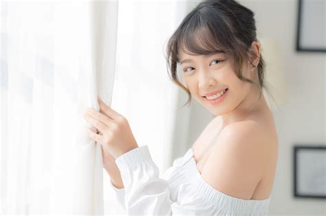아침에 일출과 함께 일어나면서 창에 서있는 아름다운 젊은 아시아 여성의 초상화 신선함과 쾌활한 라이프 스타일과 휴식 개념에 만족하는 소녀 가정 생활에 대한 스톡 사진 및
