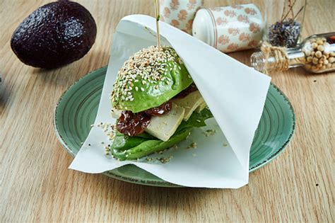 두부 치즈와 햇볕에 말린 토마토를 곁들인 만두처럼 아보카도 반으로 만든 특이한 버거 보기를 닫습니다 건강하고 녹색 음식 채식주의