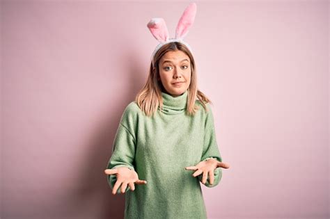 고립 된 분홍색 배경 에 서 부활절 토끼 귀를 입고 젊은 아름다운 여성은 팔과 손을 들고 단서와 혼란 스러운 표정 의심 개념 갈색 머리에 대한 스톡 사진 및 기타 이미지