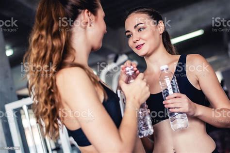체육관에서 열심히 운동 한 후 물과 휴식을 마시는 동안 함께 이야기하고 스마트 폰이나 휴대 전화를 사용하여 두 젊은 매력적인